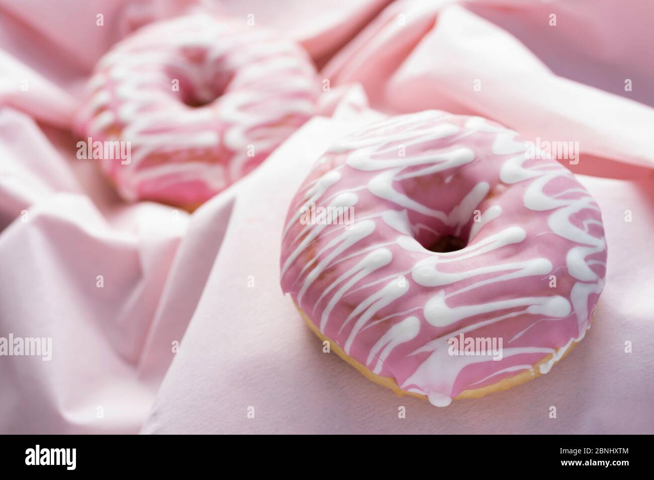 Pink glaze decorated donuts on wavy pink background in various focus ...