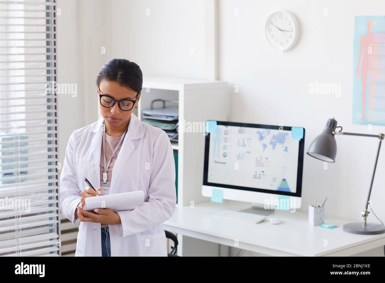 Female doctor in white coat filling medical form while standing at ...