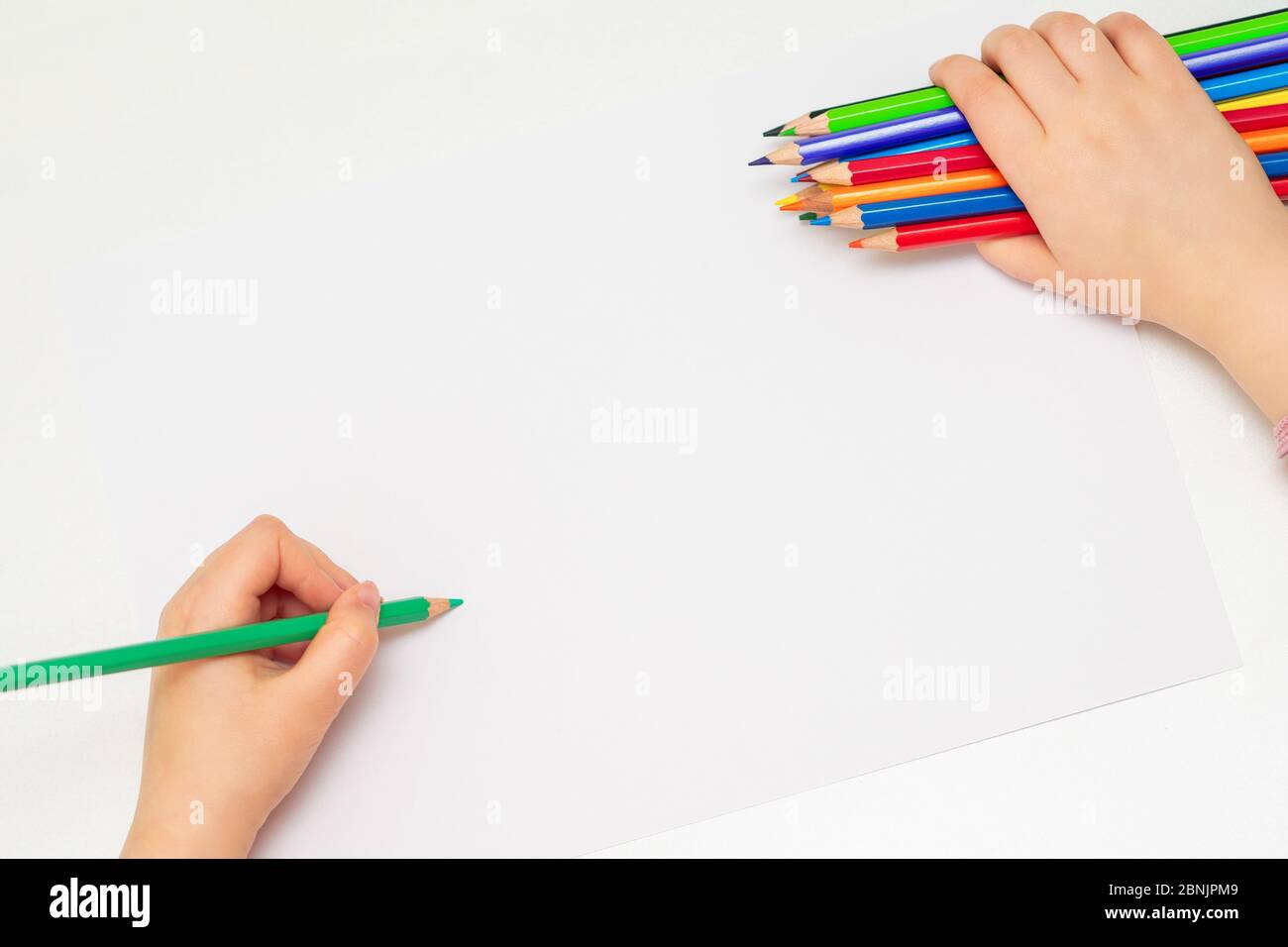 Top view of hand of child drawing by green pencil on white paper ...