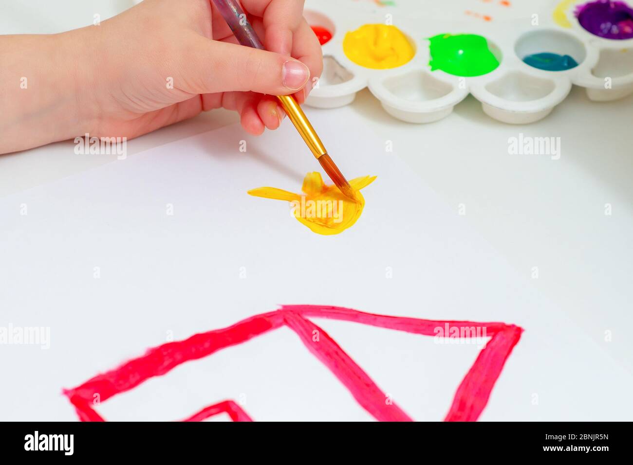 Child's hand drawing yellow sun with red house by watercolors on white ...