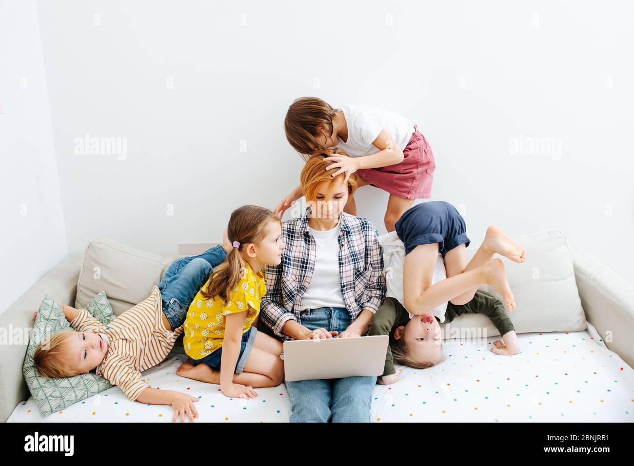 Mom working on a laptop at home while her wild kids play on top of her ...