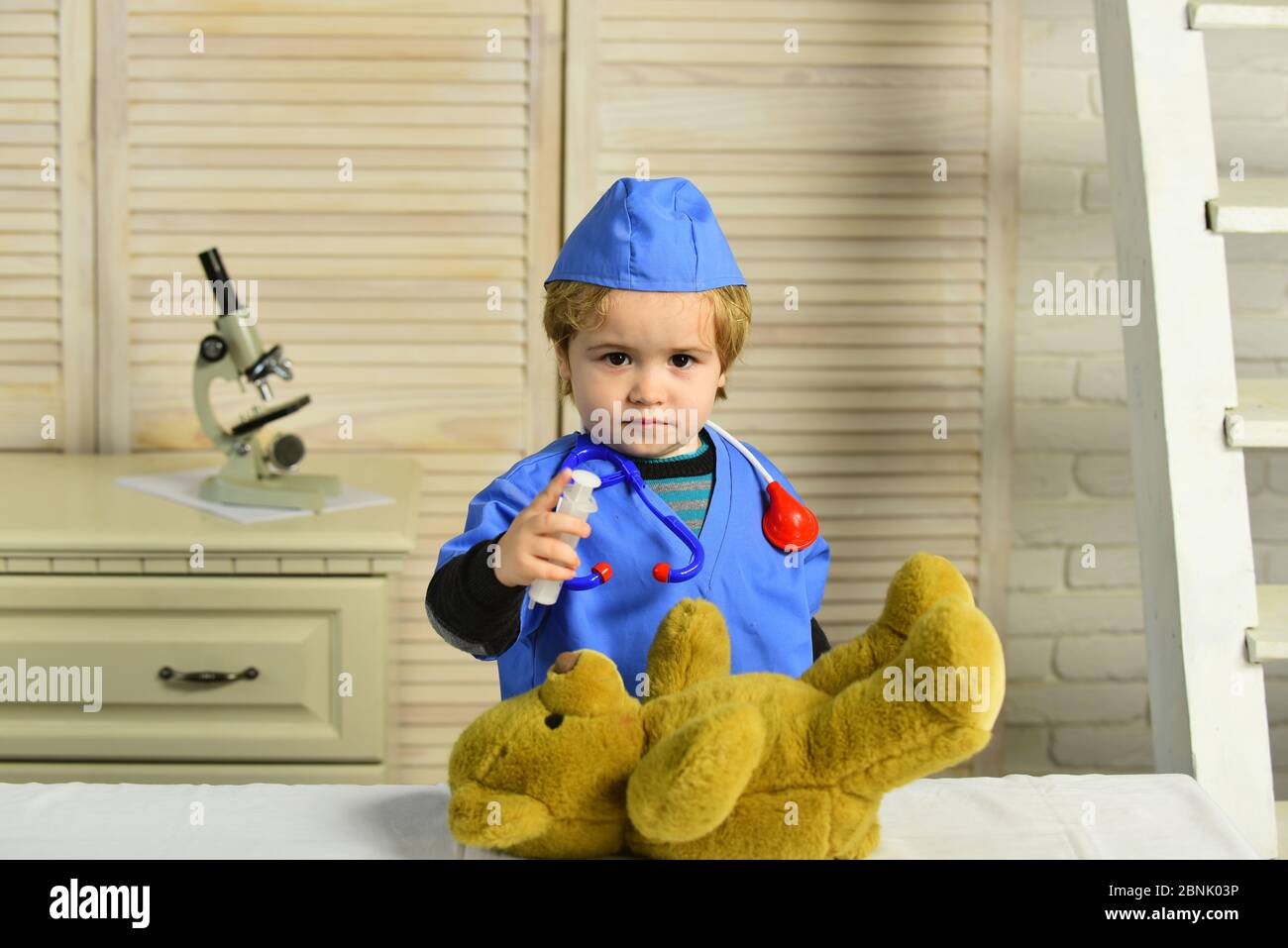 Kid in doctor coat makes injection to teddy bear. Child with serious ...