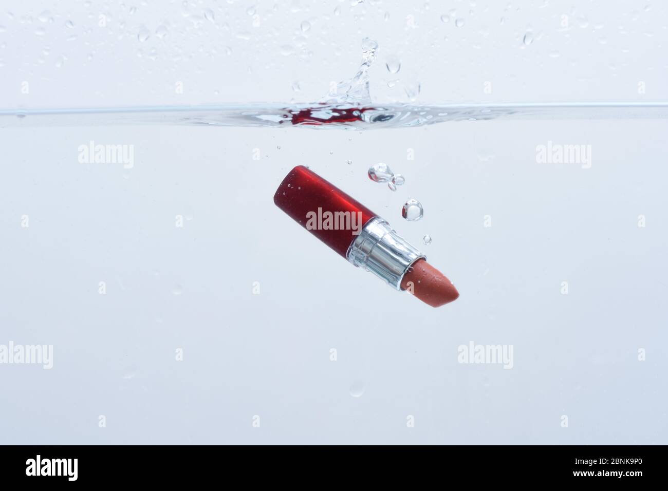 Water resisting red lipstick fall into pure, transparent water, white ...