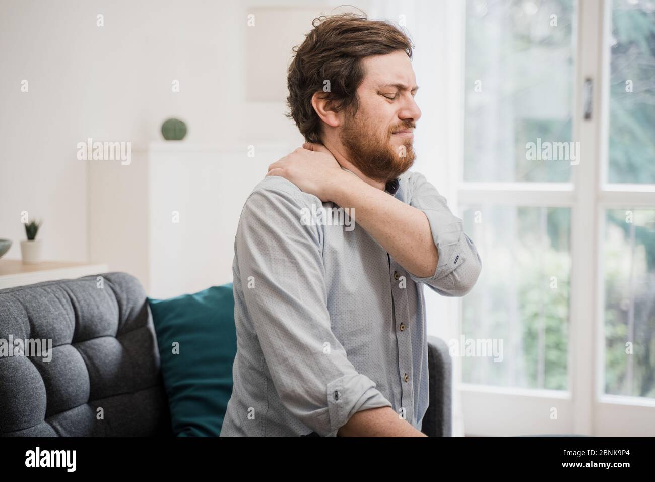 Painful guy aching from pain in back or neck at home Stock Photo - Alamy