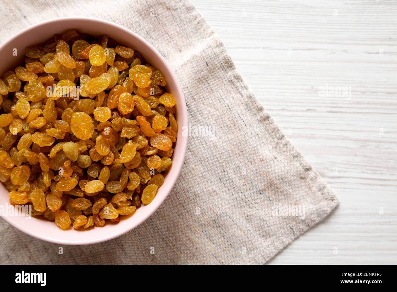 Golden Raisins in a Pink Bowl on a white wooden background, top view ...