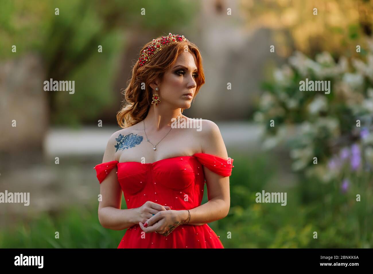 Portrait of attractive redhead tattooed woman in red dress and diadema ...