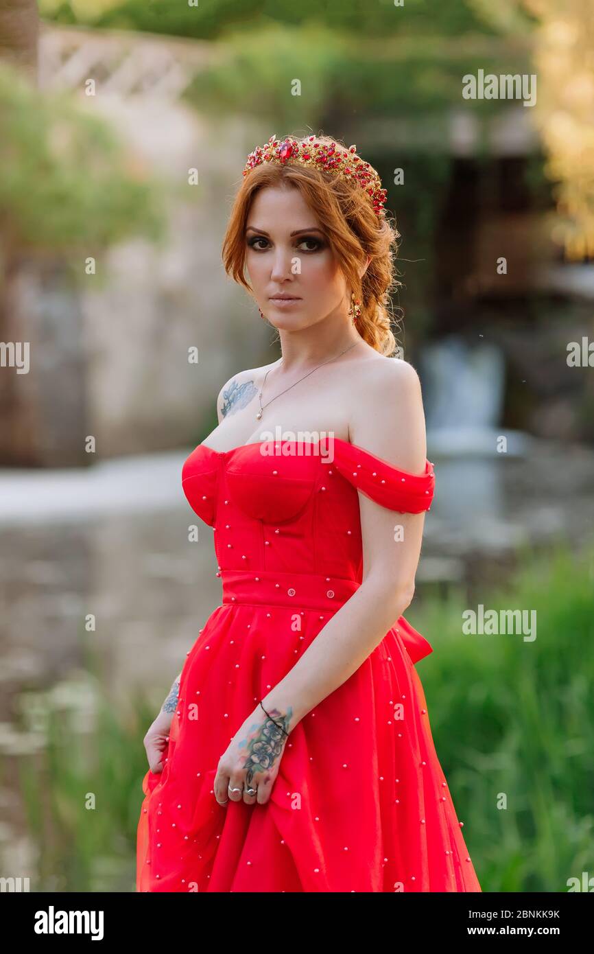 Portrait of attractive redhead tattooed woman in red dress and diadema ...
