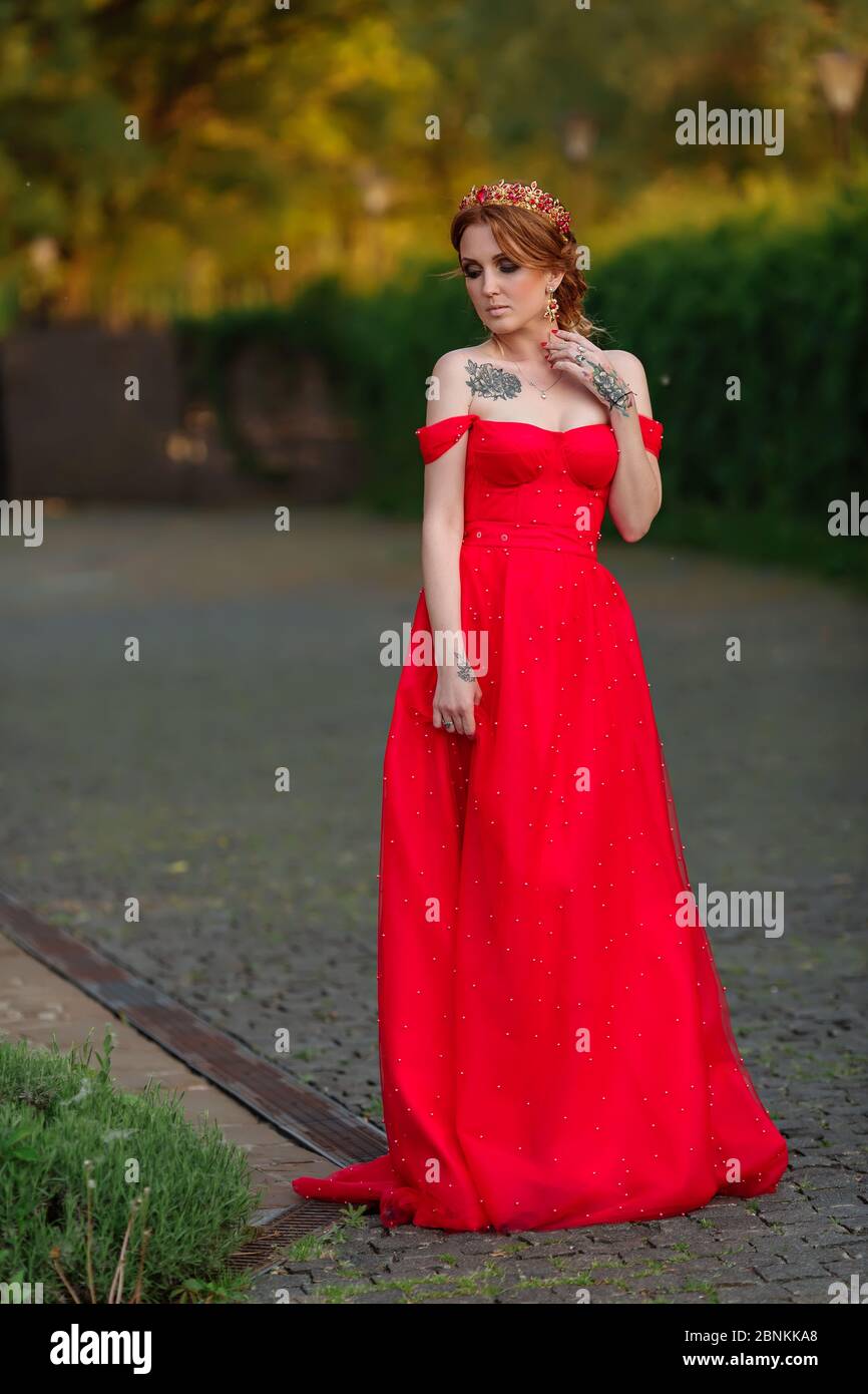 Attractive redhead tattooed woman in red dress and diadema on her head ...