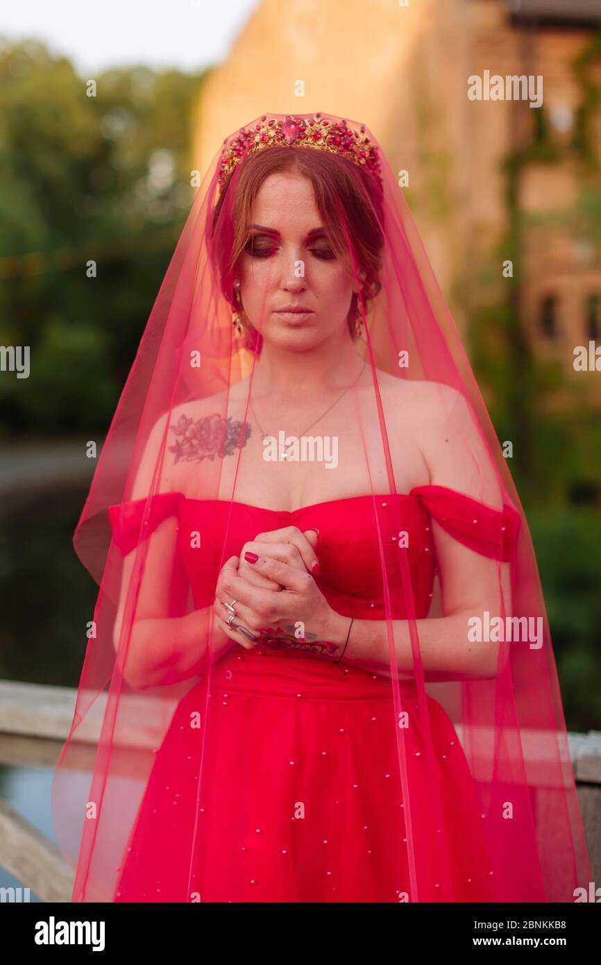 Portrait of attractive redhead tattooed woman in long red dress ...