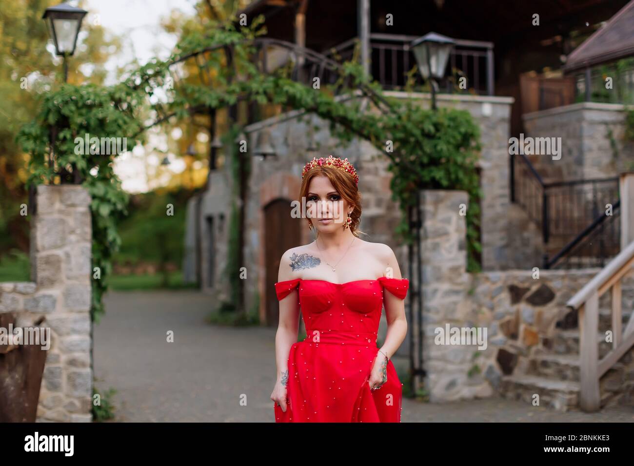 Portrait of attractive redhead tattooed woman in red dress and diadema ...