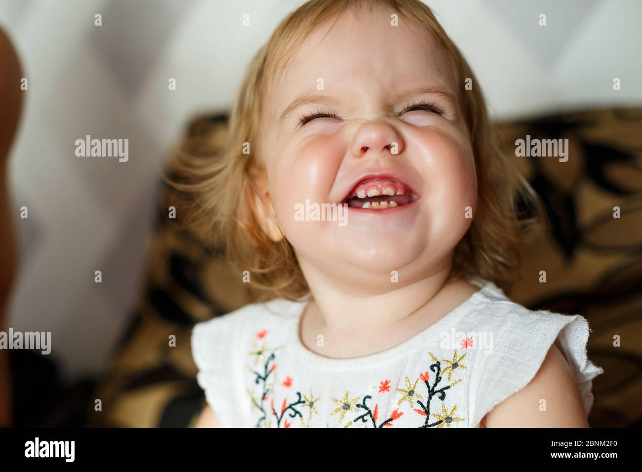 A 2 years old girl is sitting on the bed and smiling. The child ...