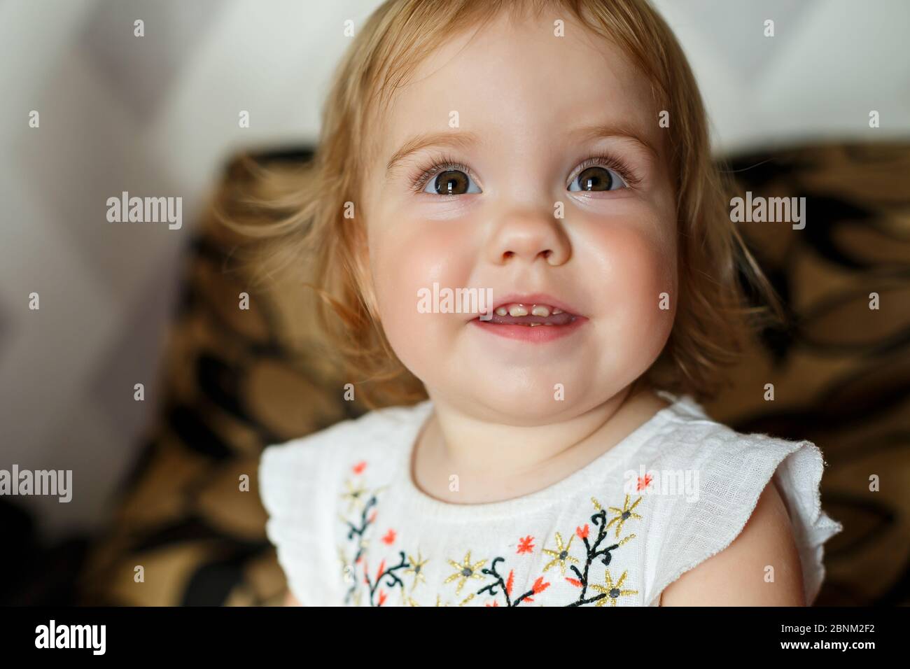A 2 years old girl is sitting on the bed and smiling. The child ...