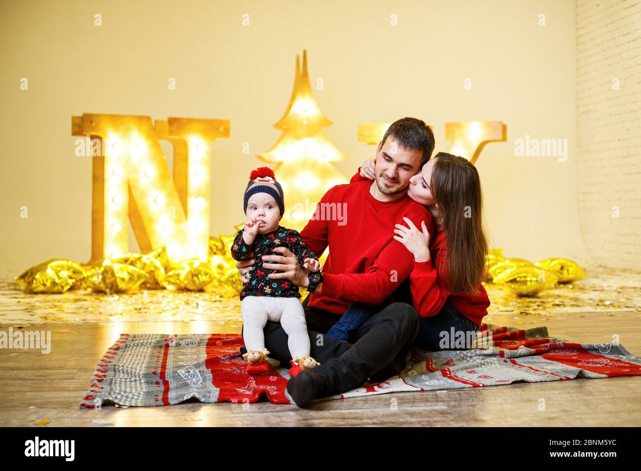 A happy family in red sweaters is sitting together on the floor ...