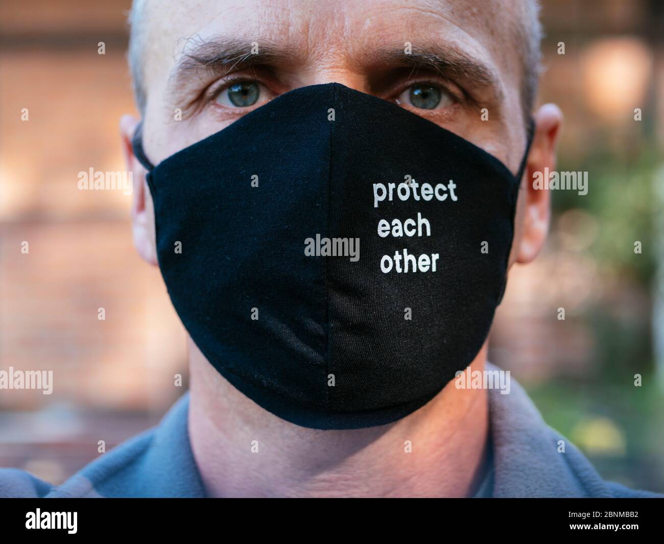 Man wearing a community face mask with the message to protect each ...