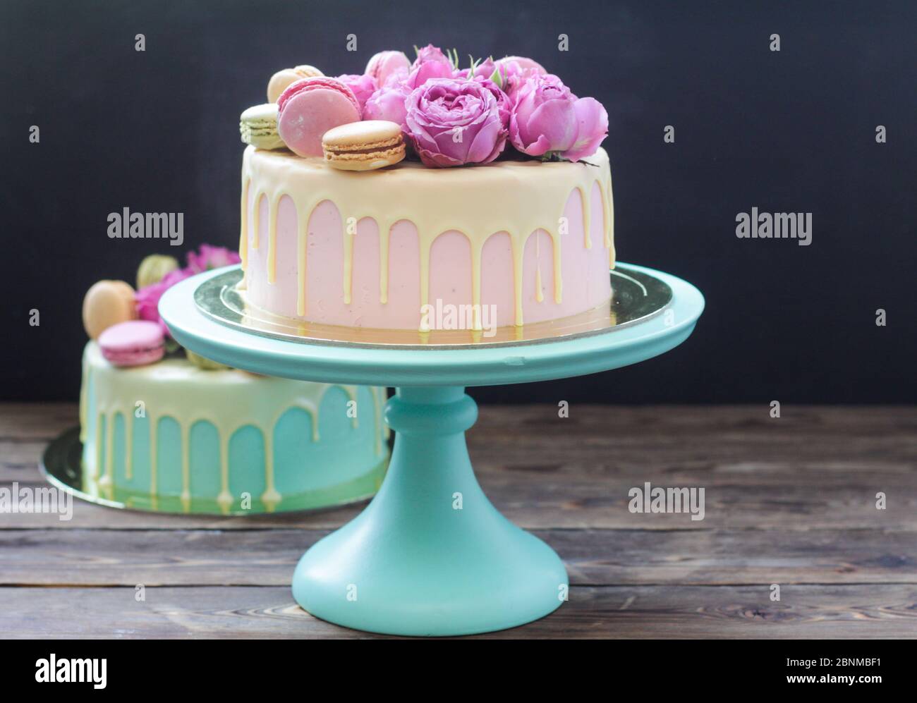 Modern pink cake with melted chocolate, fresh roses and macaroons ...