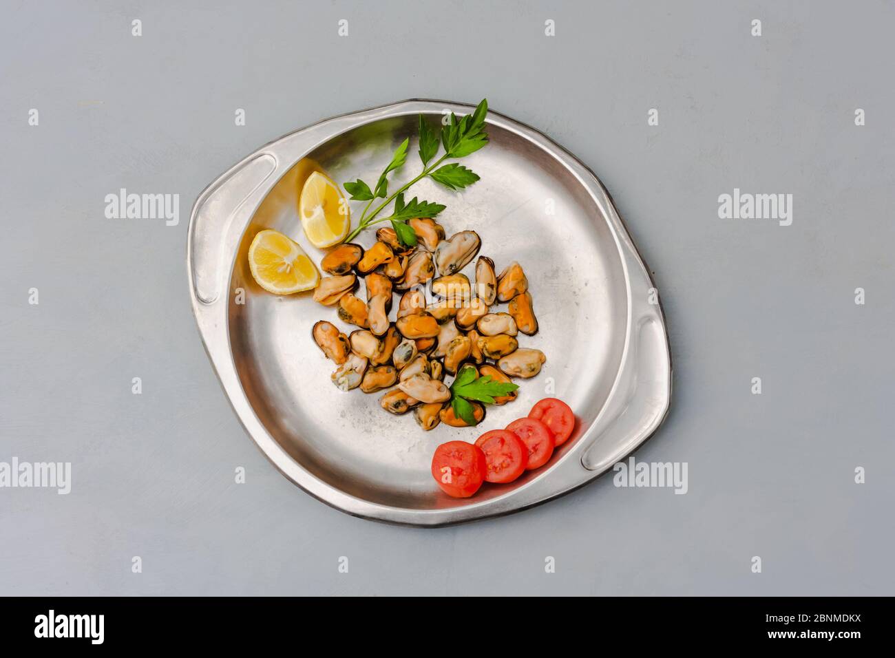 Mussels without shell with tomato slices and lemon on a steel tray ...