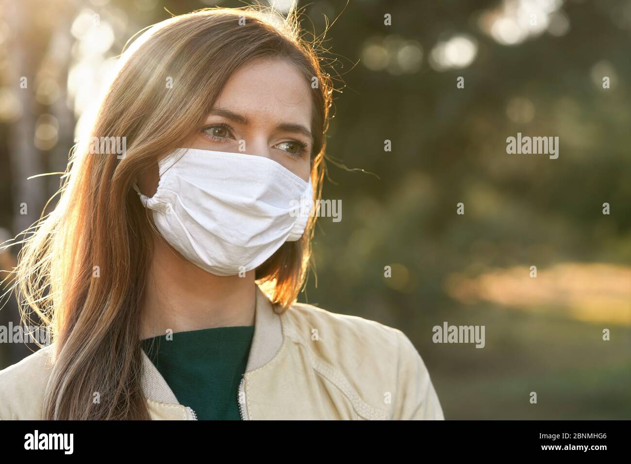 Young woman wearing white cotton virus mouth nose mask, blurred sunset ...