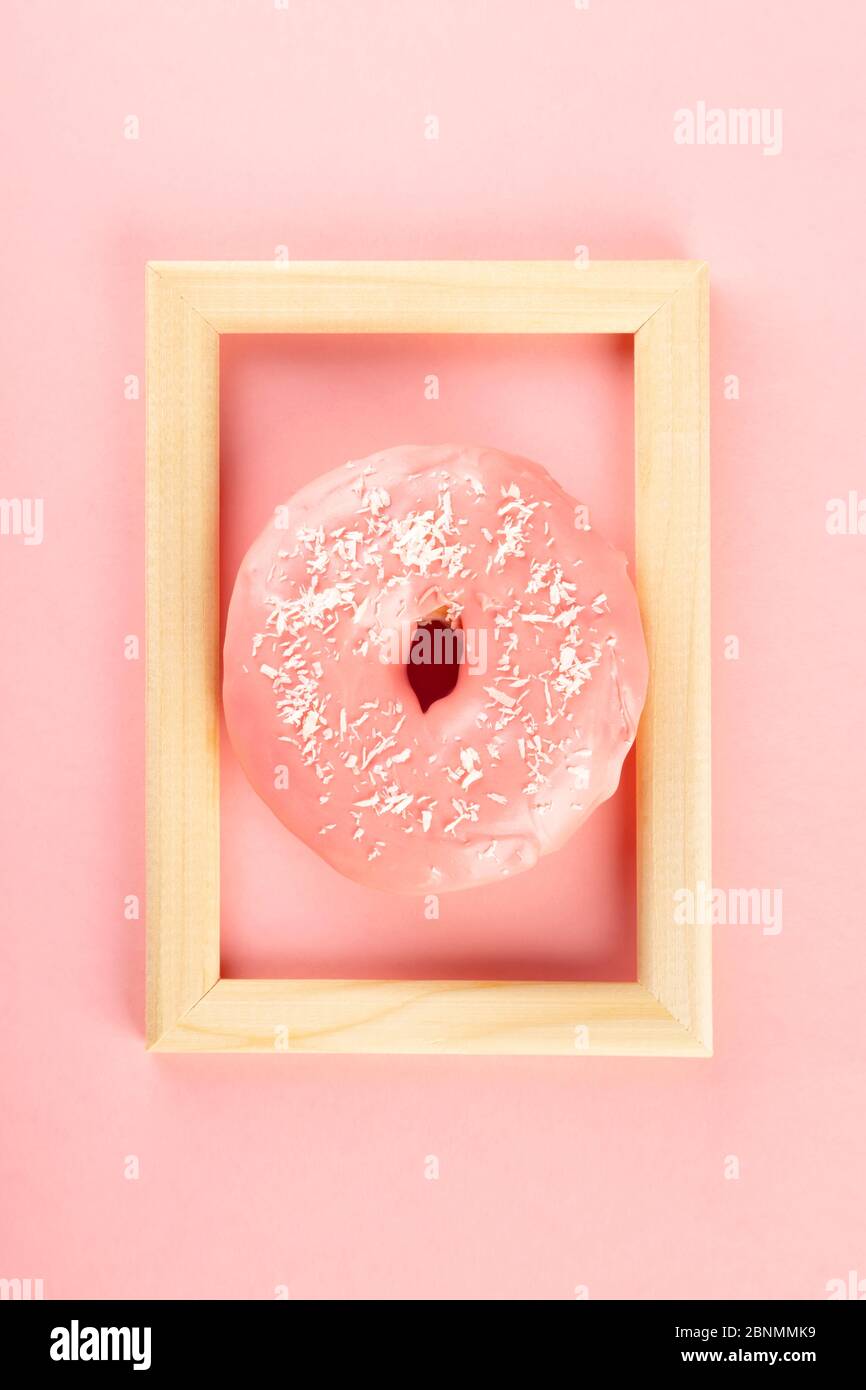 Donut with pink icing and coconut pastry topping in wooden frame on ...