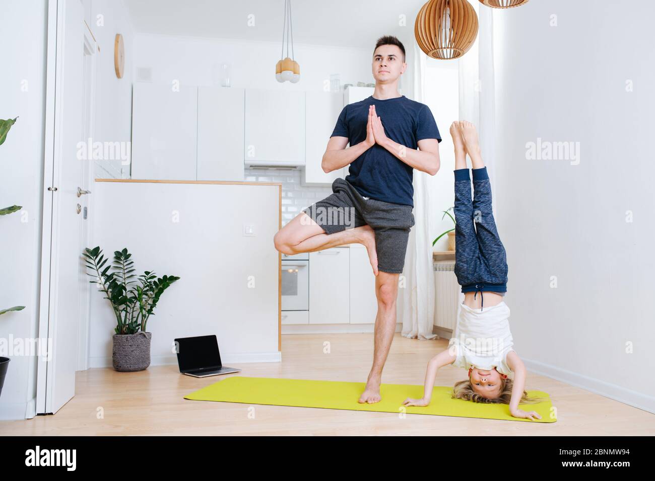 Father and son doing yoga at home on a mat. Headstand and one leg stand ...