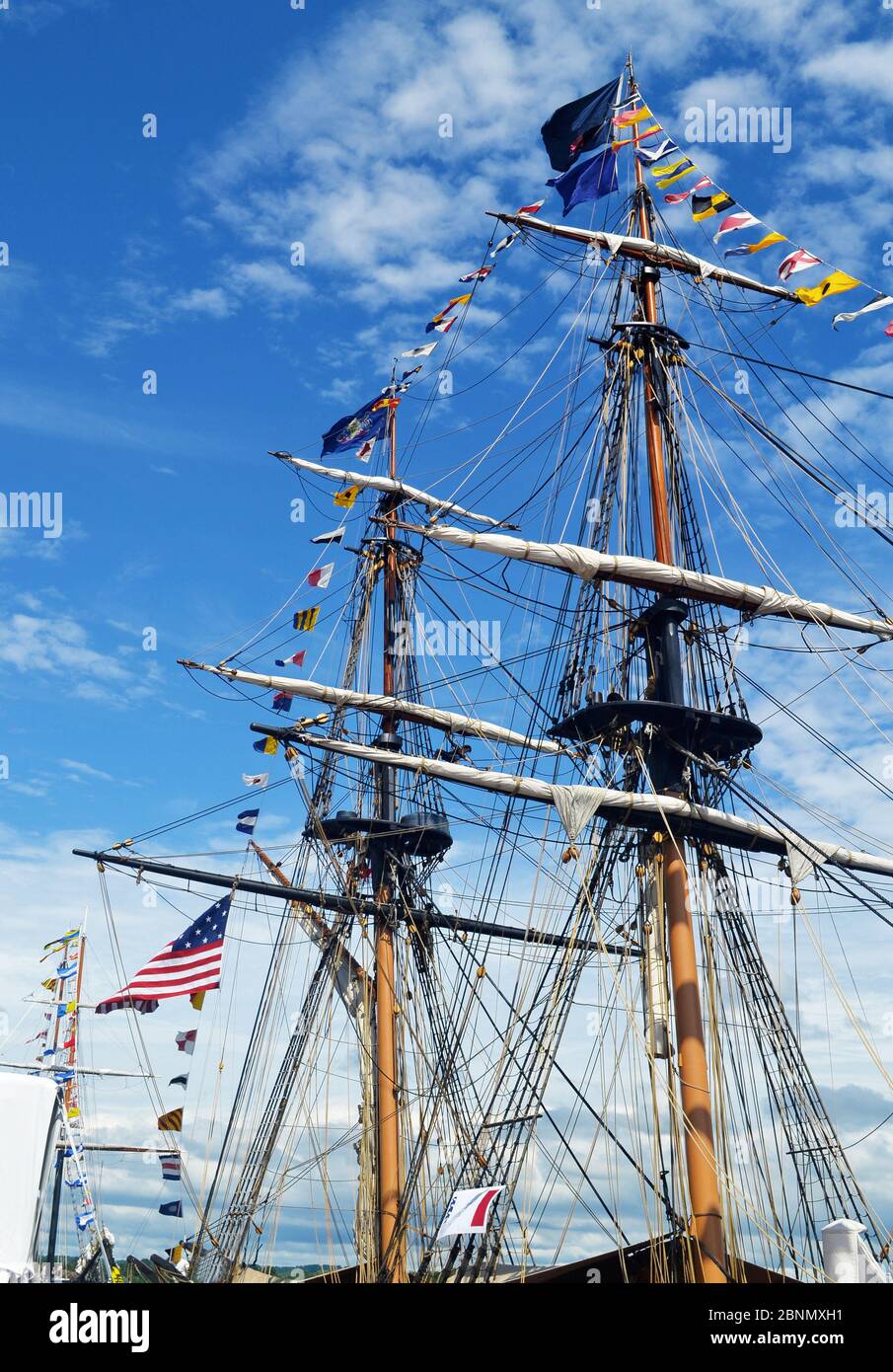 The tall mast of a big tall ship with all the flags under a blue sky ...