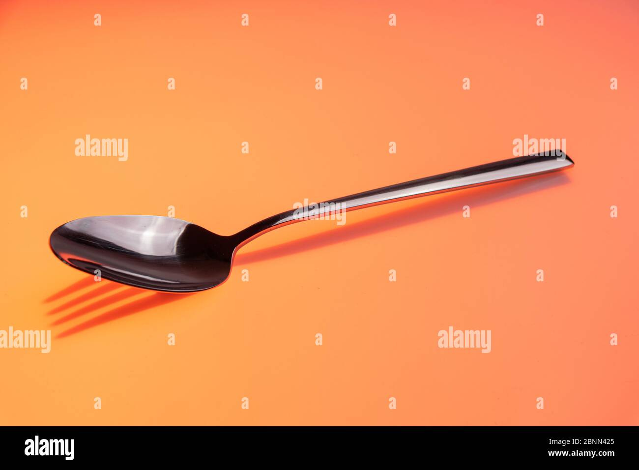 Metal spoon casting a fork shadow on orange background Stock Photo - Alamy