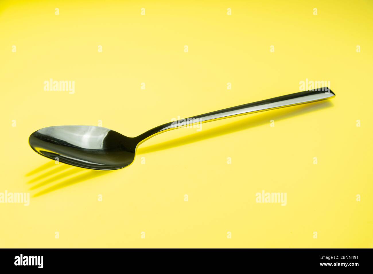 Metal spoon casting a fork shadow on yellow background Stock Photo - Alamy