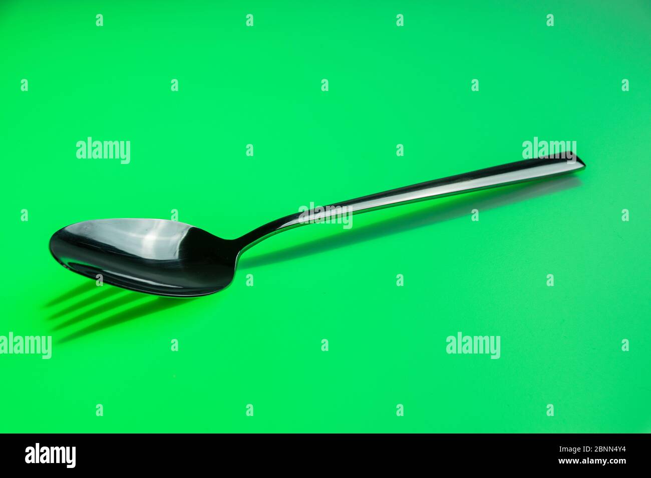 Metal spoon casting a fork shadow on green background Stock Photo - Alamy