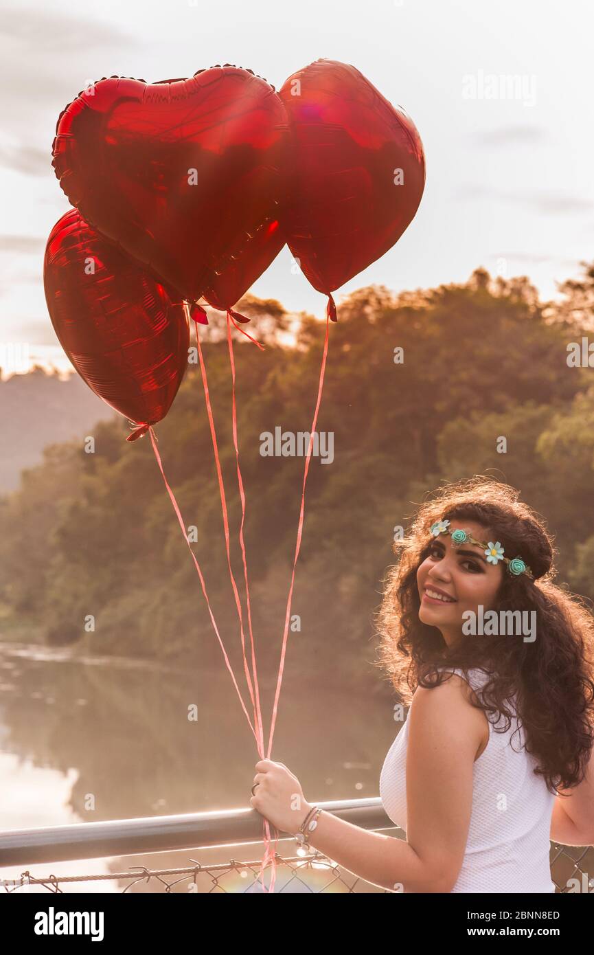 Pretty girl holding red balloons in heart shape looking at the camera ...