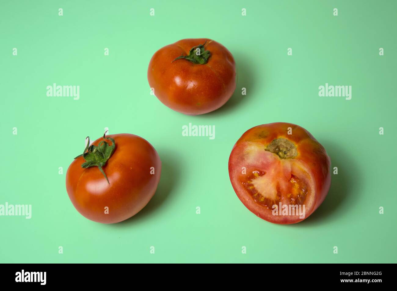 Two whole tomatoes and one match on green background Stock Photo - Alamy