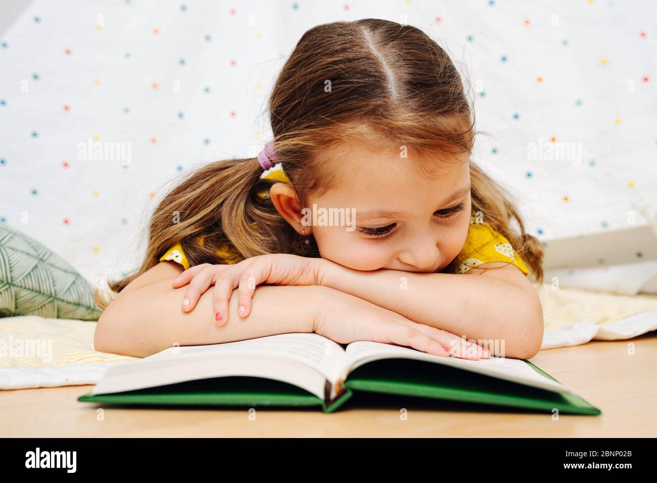 Entertained little girl keen on reading book while lying on the floor ...