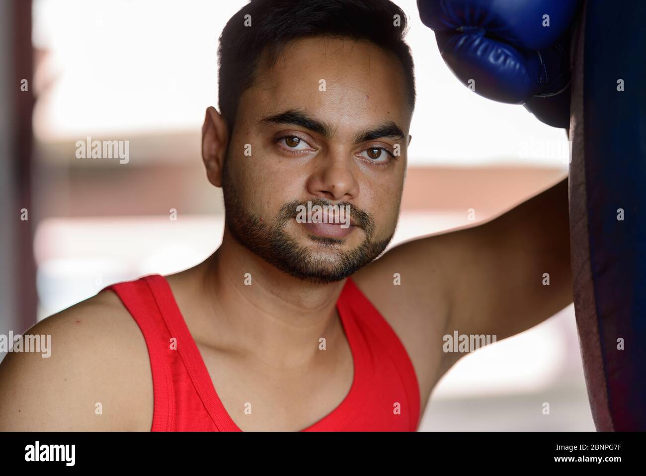Face of young handsome bearded Indian man as boxer training at the gym ...