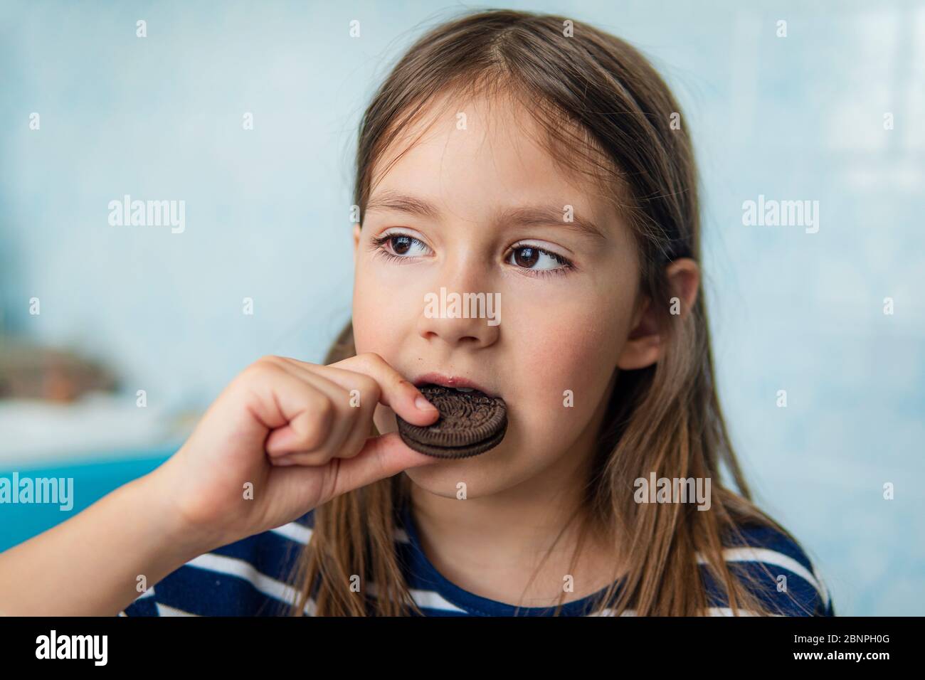 Close up of a girl eating a round chocolate cookie in the kitchen at ...