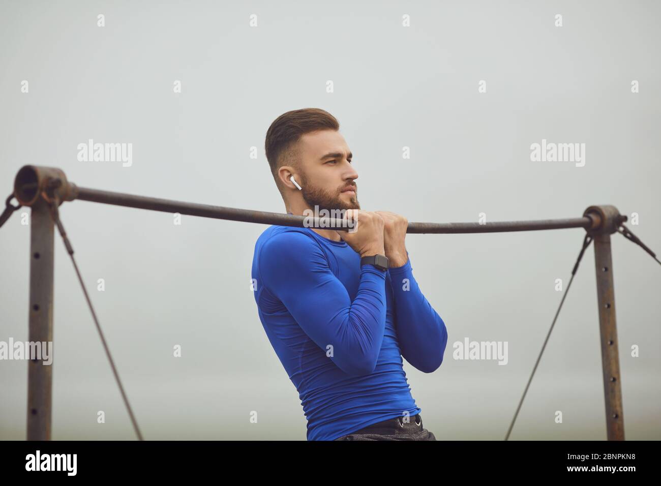 A bearded guy doing pull-ups on a horizontal bar in a stadium in the ...