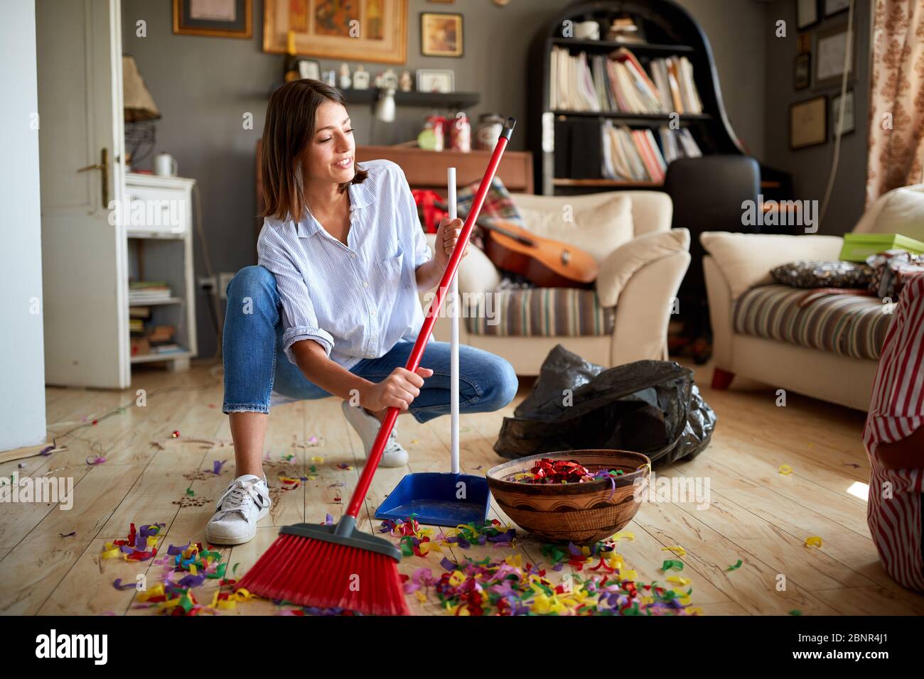 Young female cleaning with broom after party Stock Photo - Alamy