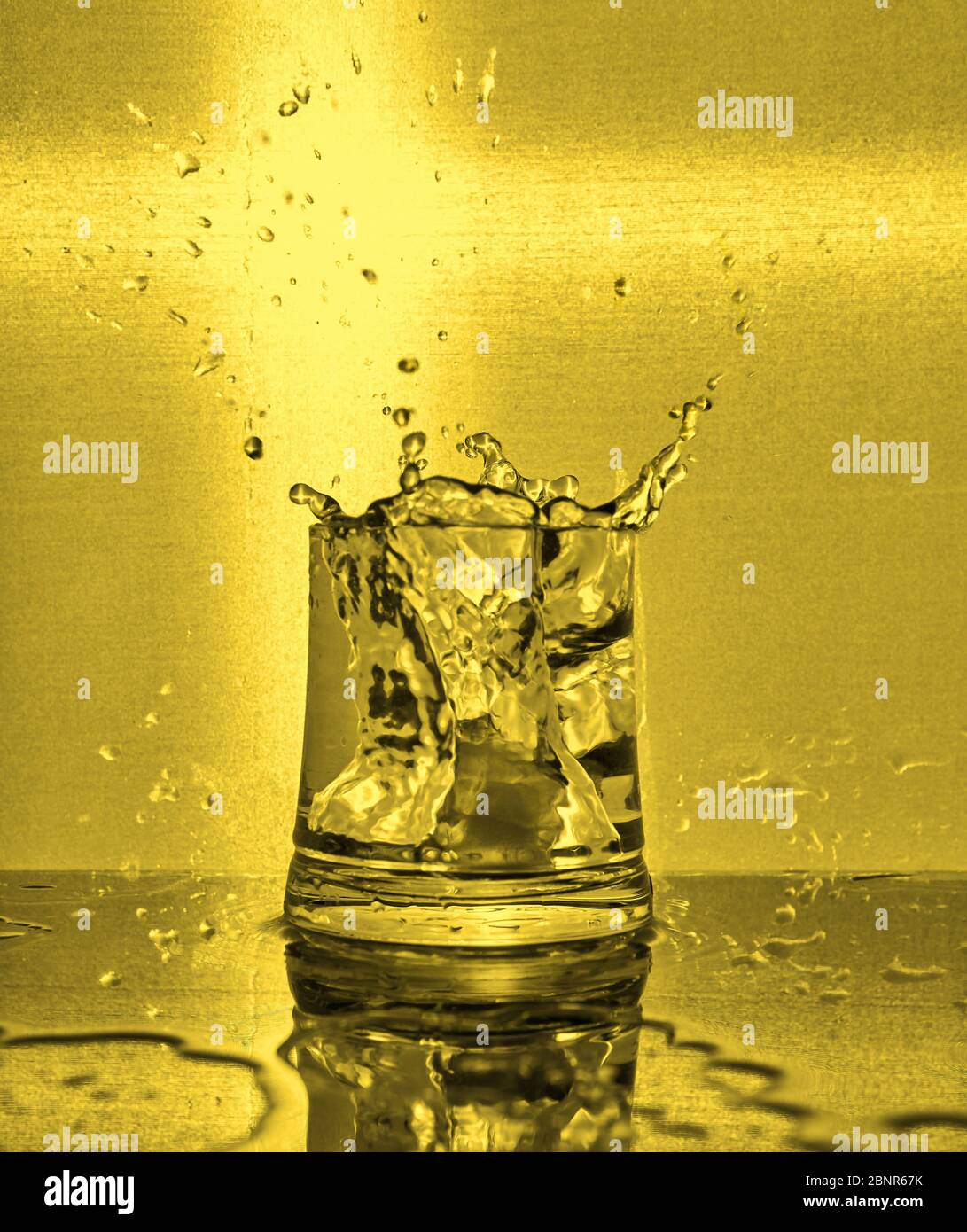 Ice cubes splashing into glass of water. Yellow background Stock Photo ...