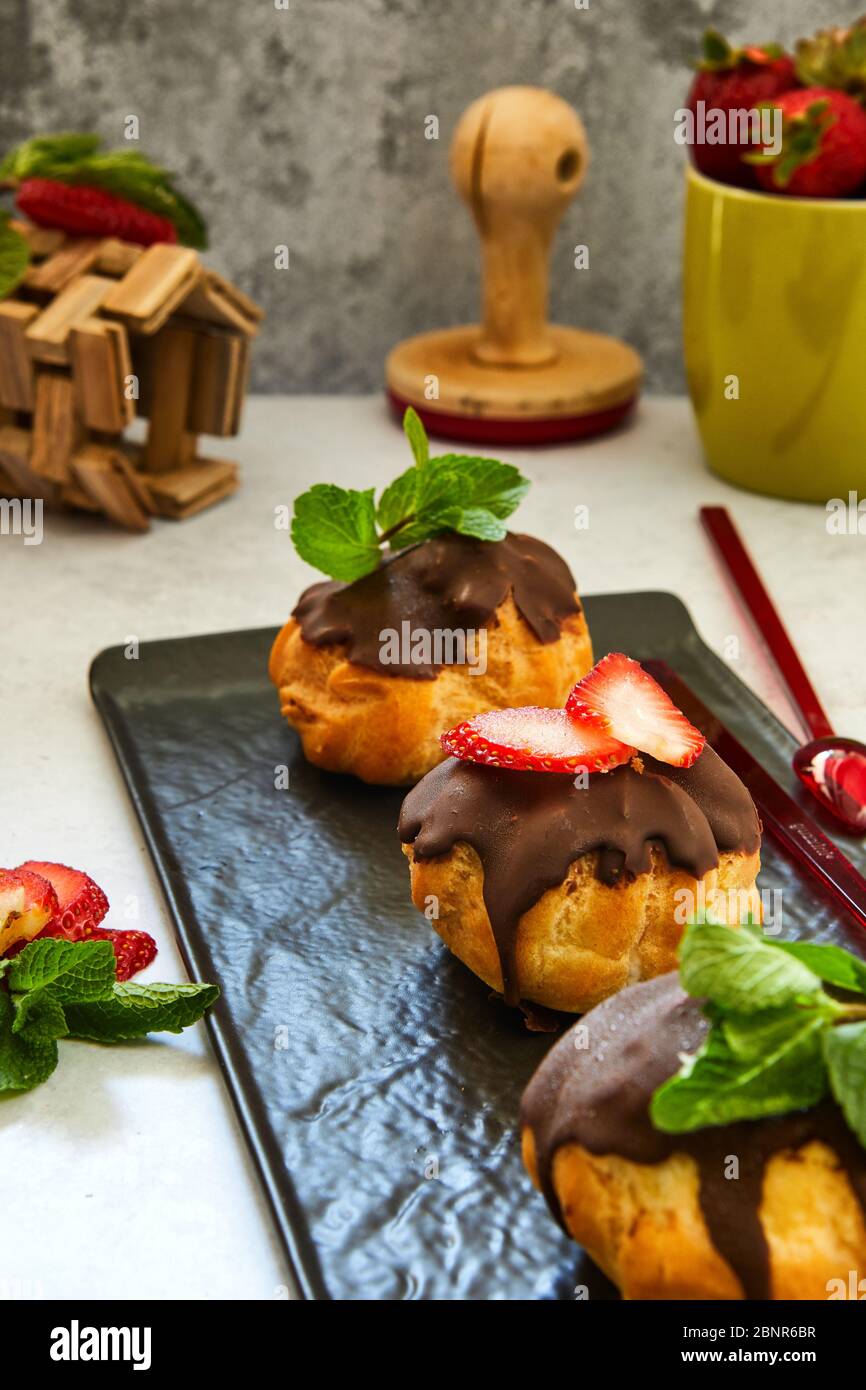 Stack eclair of profiteroles with dark melted chocolate on a black dish ...