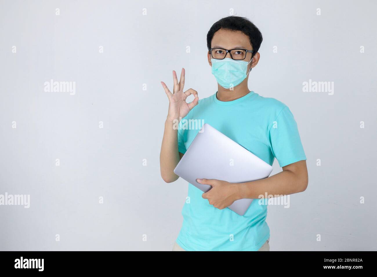 Young Asian Man wear medical mask is carrying a laptop with ok hand ...