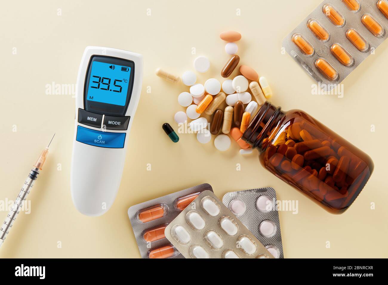 Infrared thermometer with medical pills and syringe on yellow ...