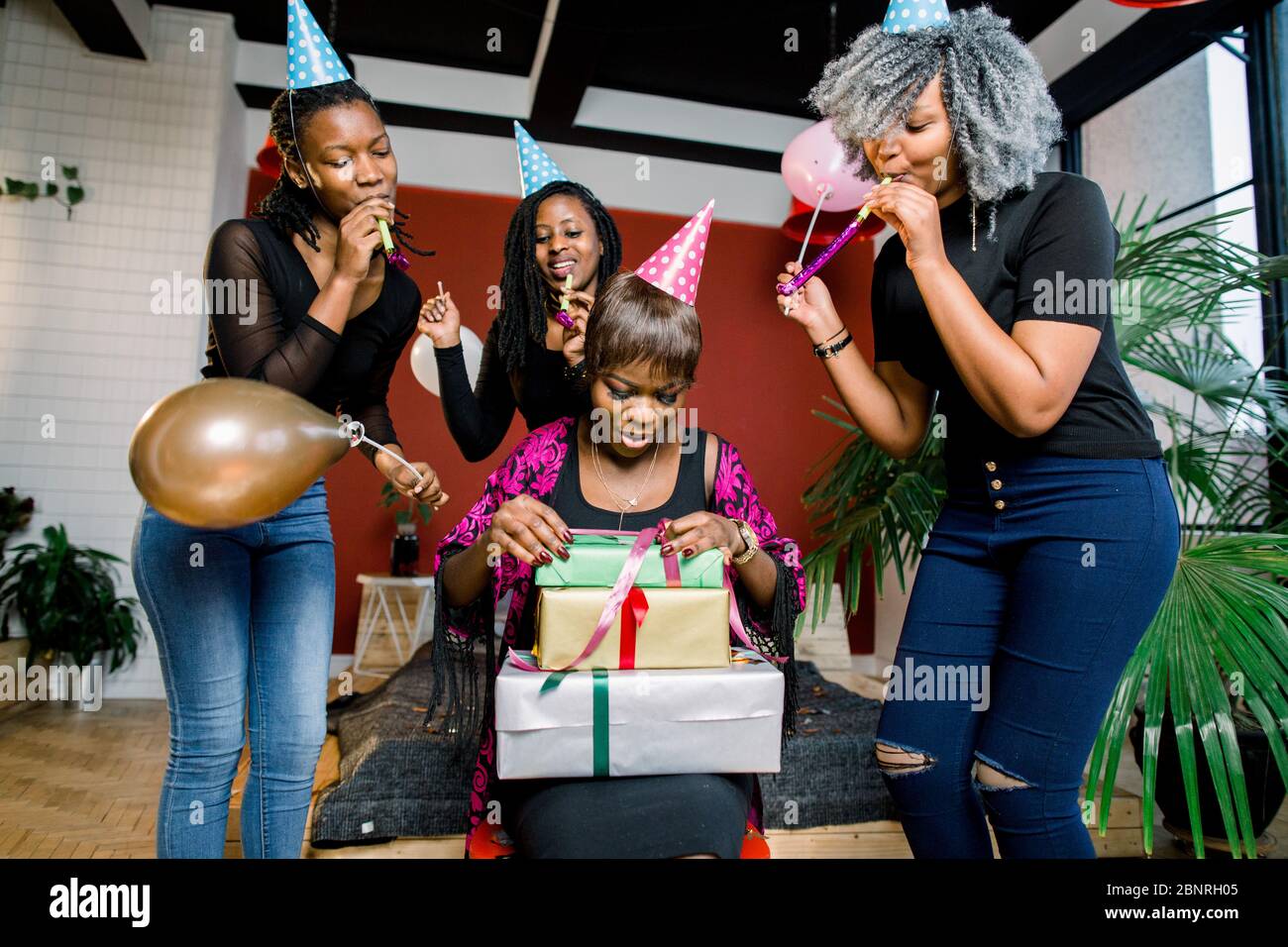 A beautiful smiling African girl opens a present at her birthday party ...