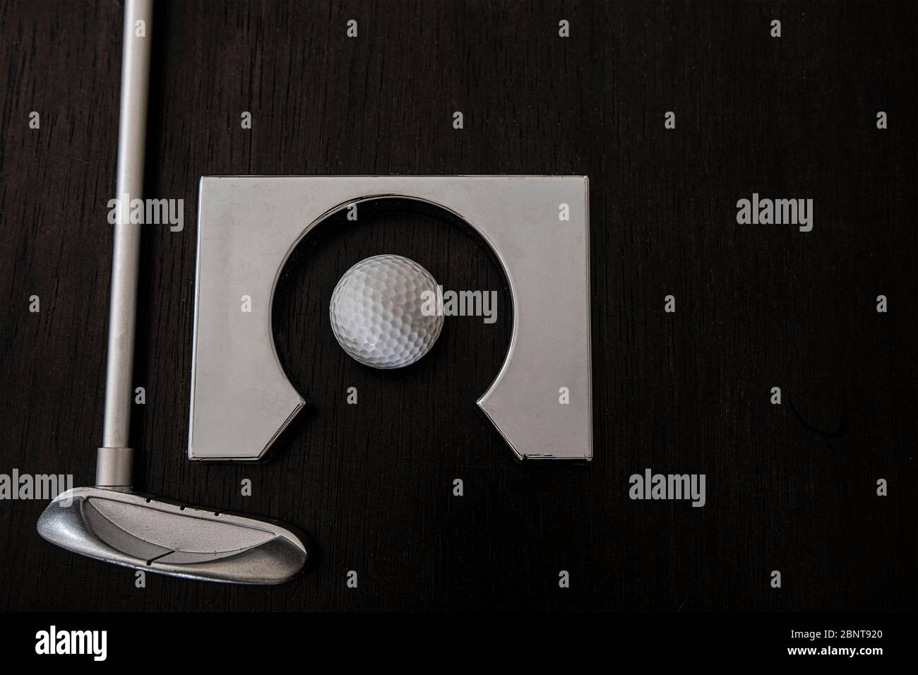 Metal golf club next to a golf ball and a hole frame to play on a black ...