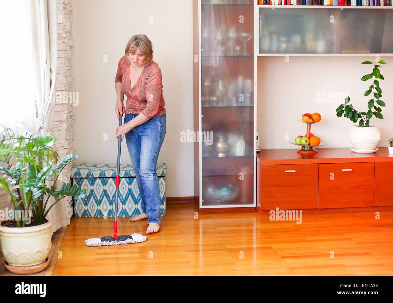 Full body mature barefoot woman using mop to wash floor while cleaning ...