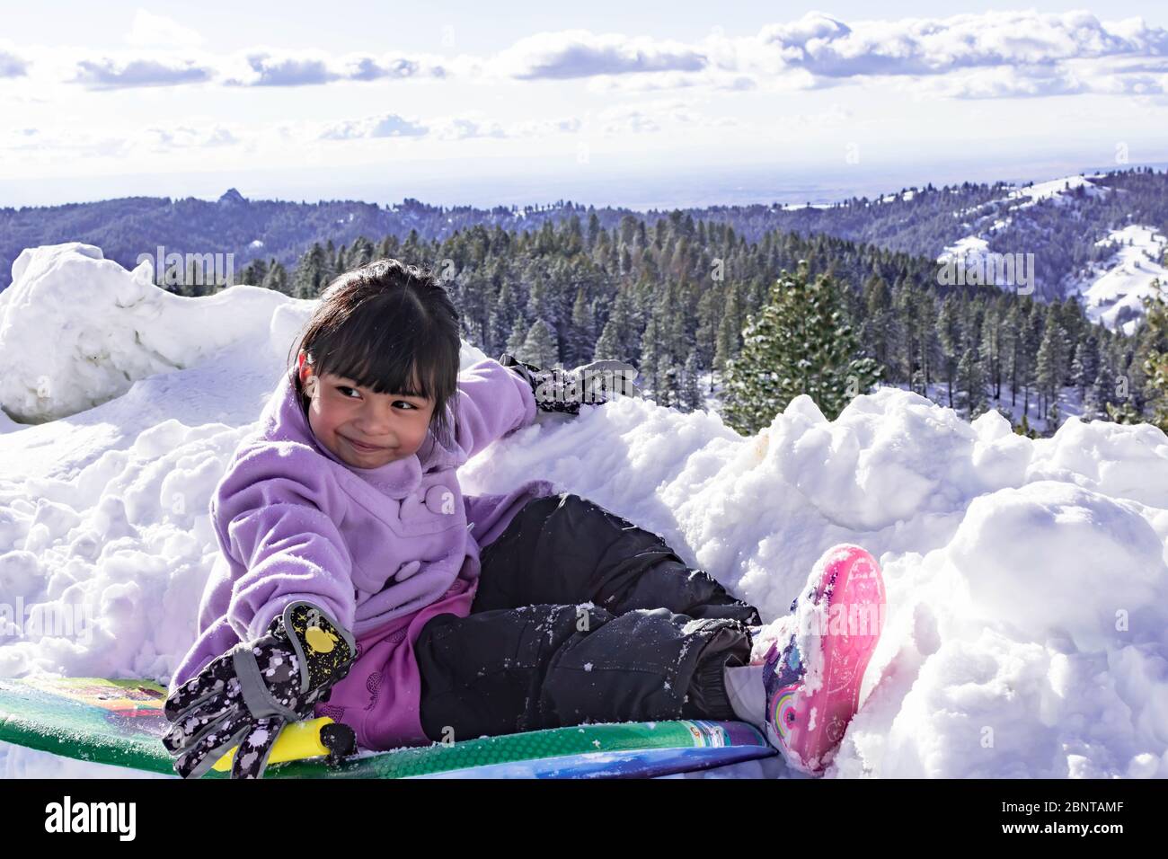 Female child while sitting on a snow board and playing with snow Stock ...