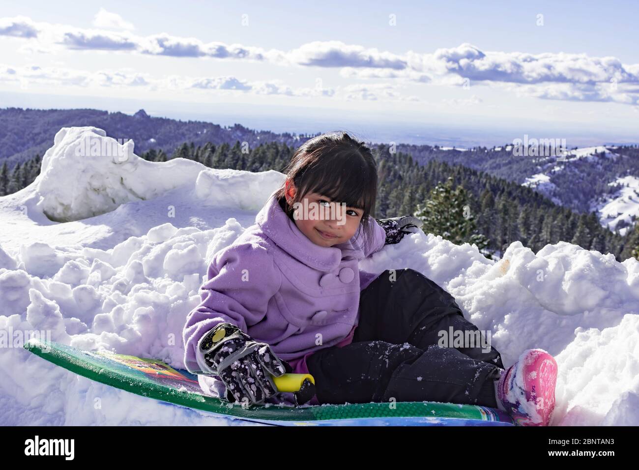Female child while sitting on a snow board and playing with snow Stock ...