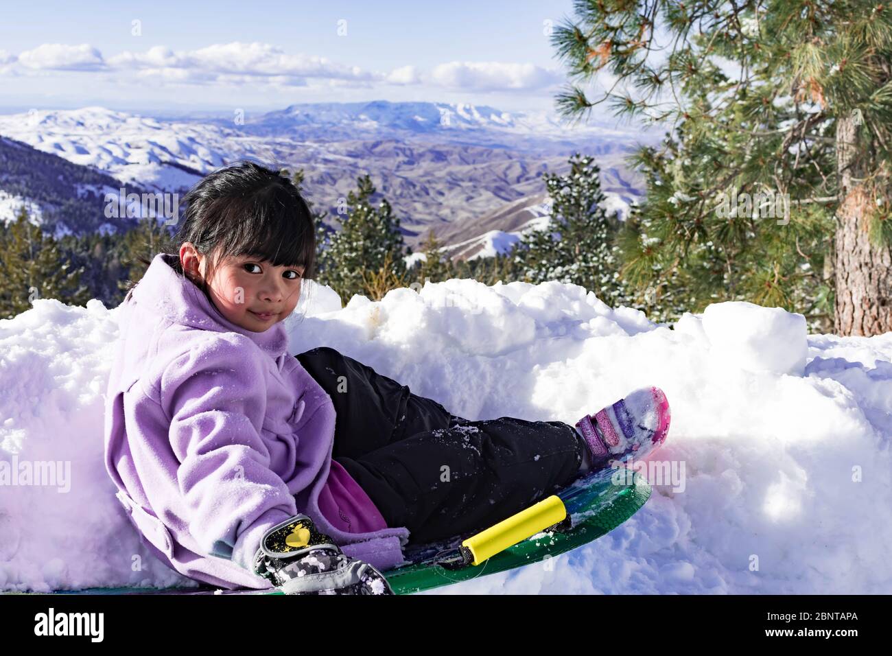 Female child while sitting on a snow board and playing with snow Stock ...