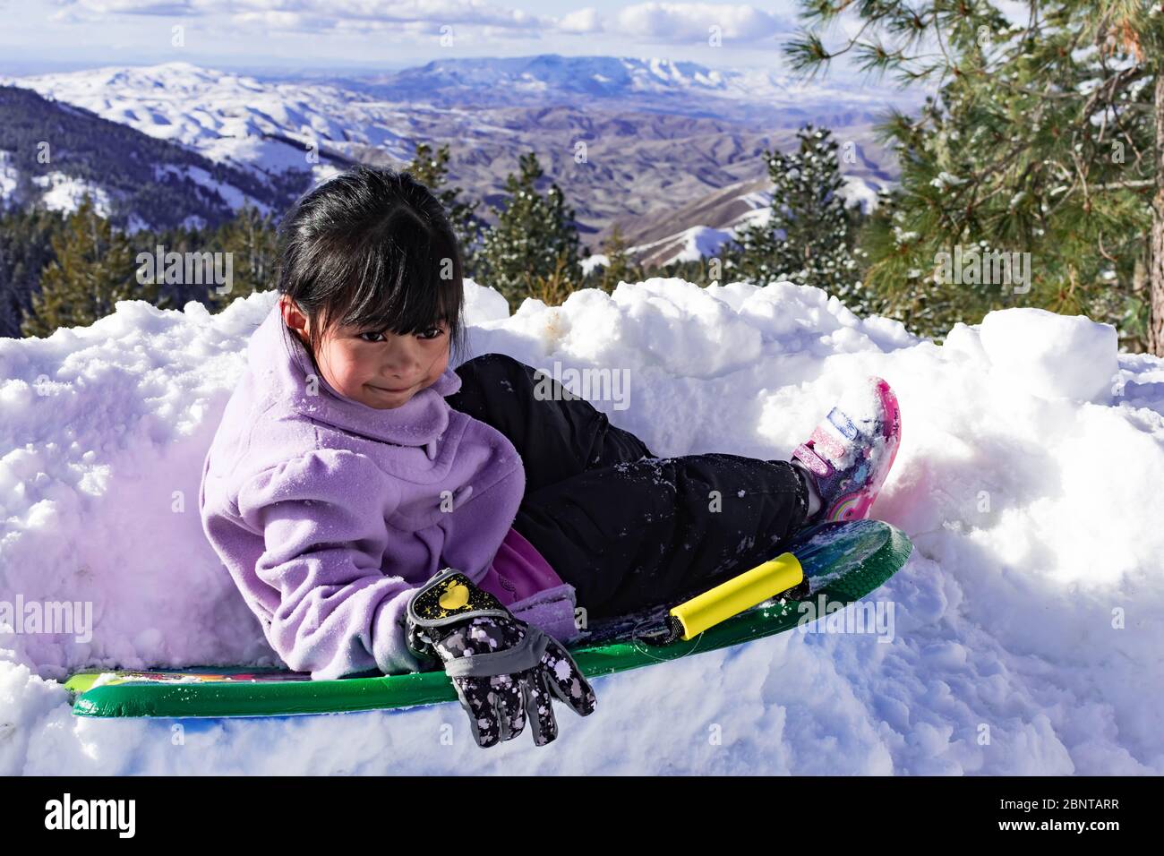 Female child while sitting on a snow board and playing with snow Stock ...