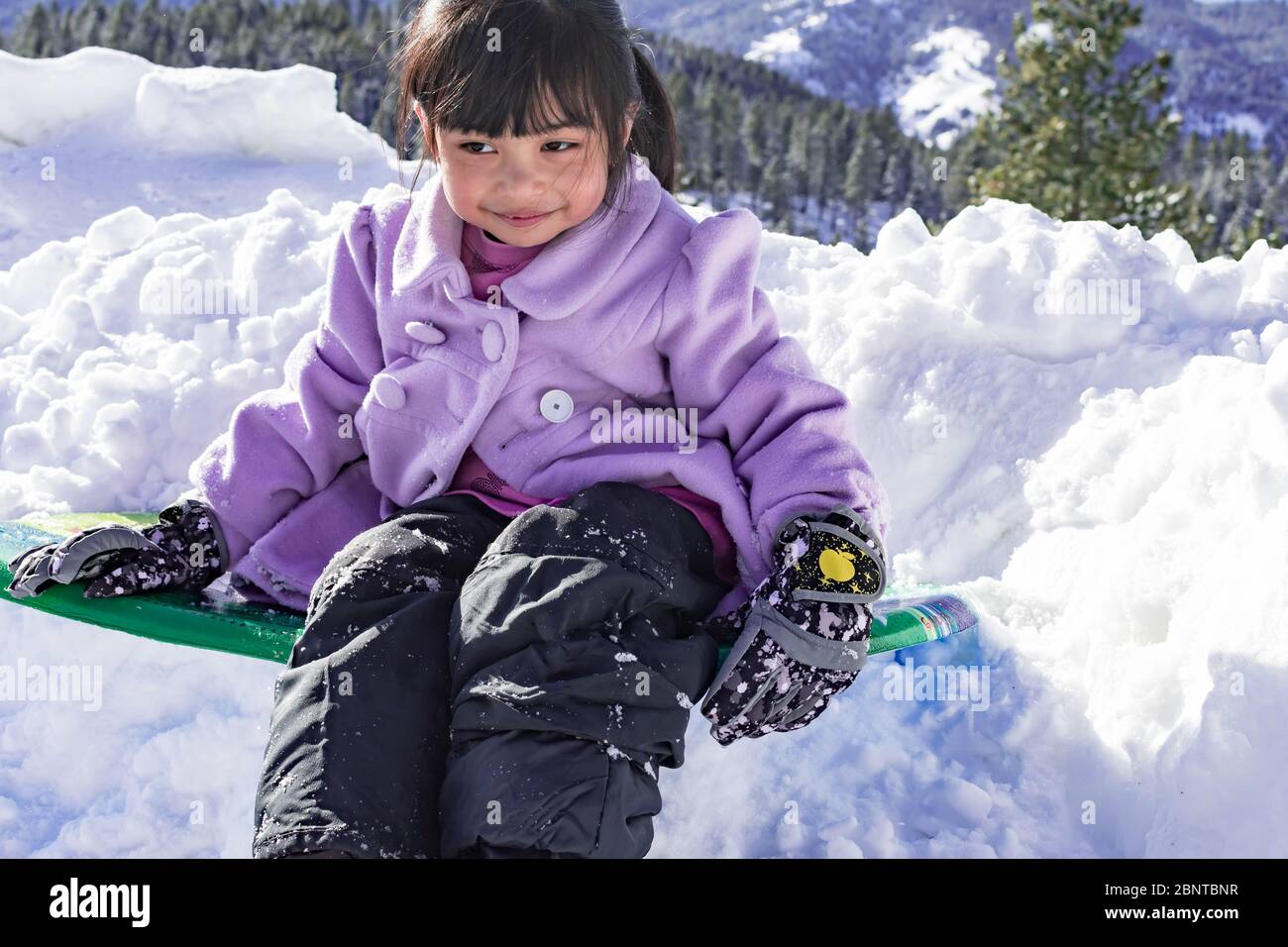 Female child while sitting on a snow board and playing with snow Stock ...