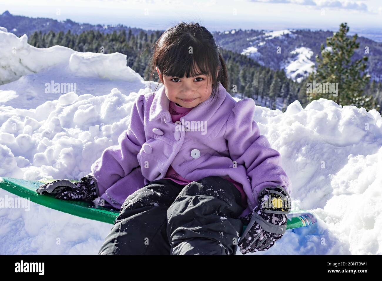 Female child while sitting on a snow board and playing with snow Stock ...
