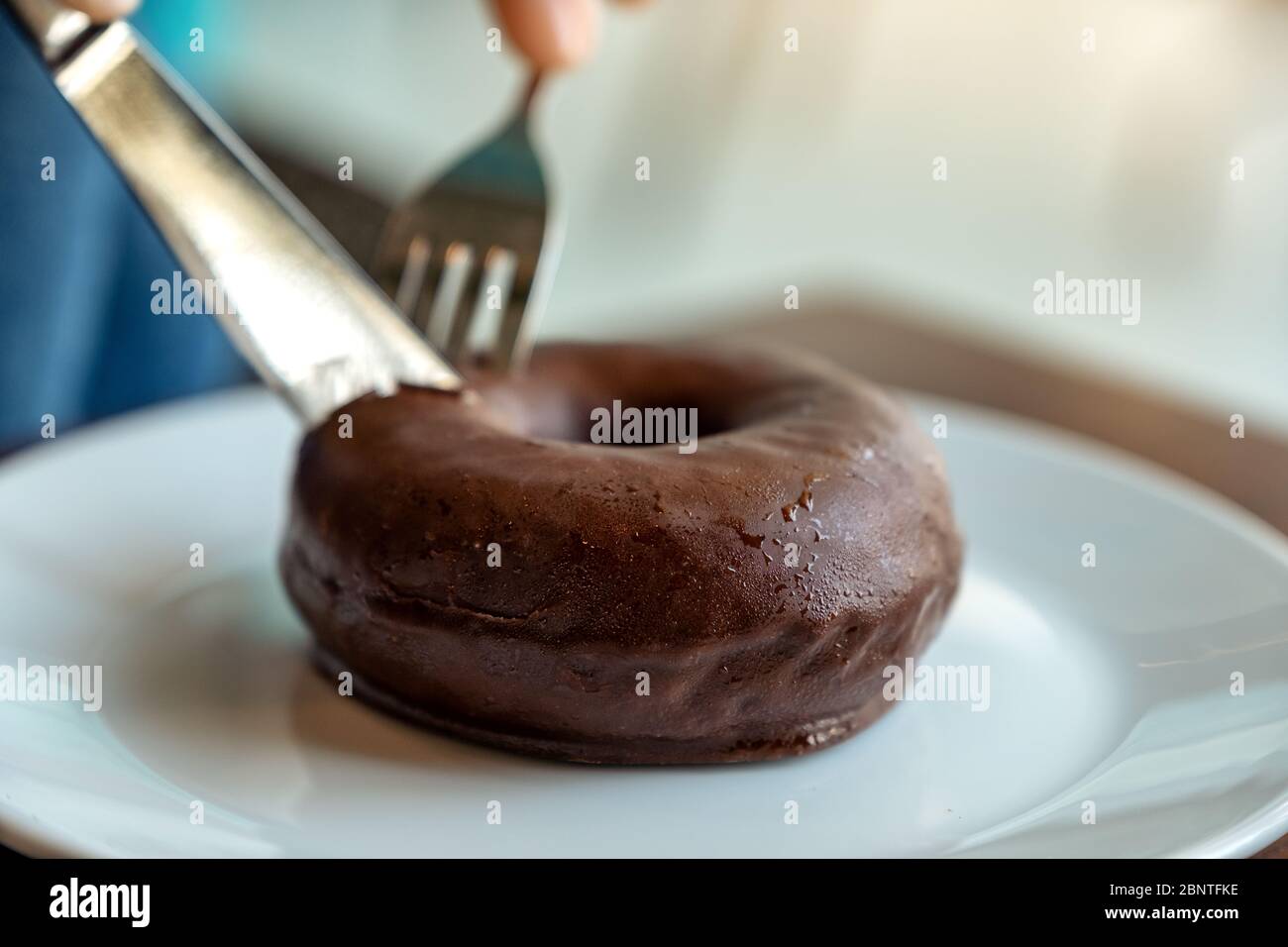 Closeup image of hands cutting a piece of chocolate donut by knife and ...