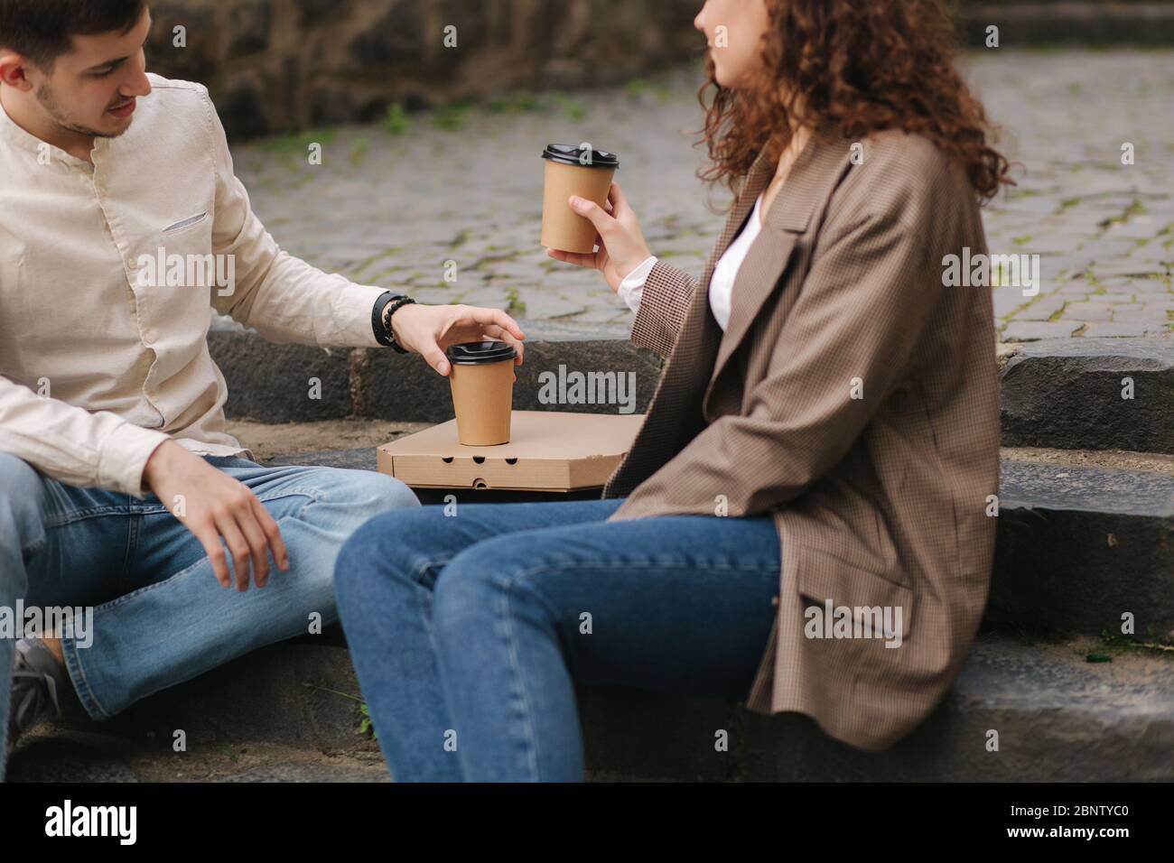 Smiling love couple sitting on the stairs outdoors and hold cups of ...
