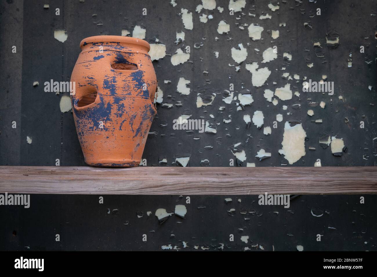 Old terracotta clay pot on a wood shelf with peeling paint texture ...